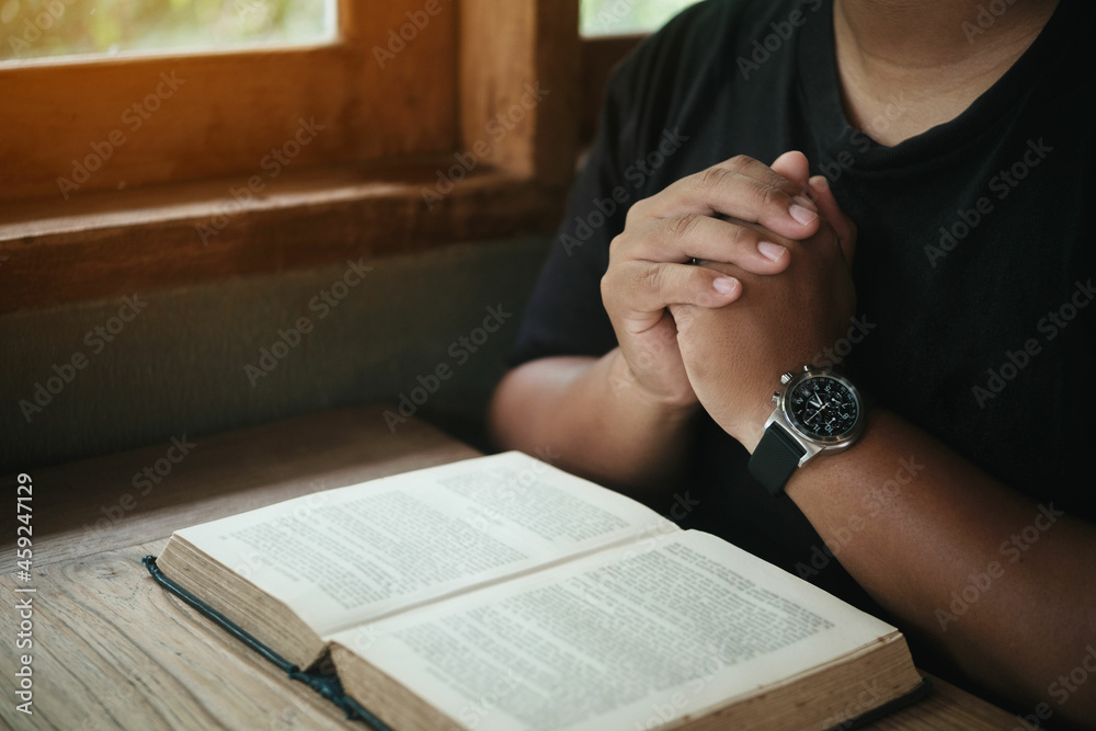 Man with Bible praying, hands clasped together on her Bible on wooden ...