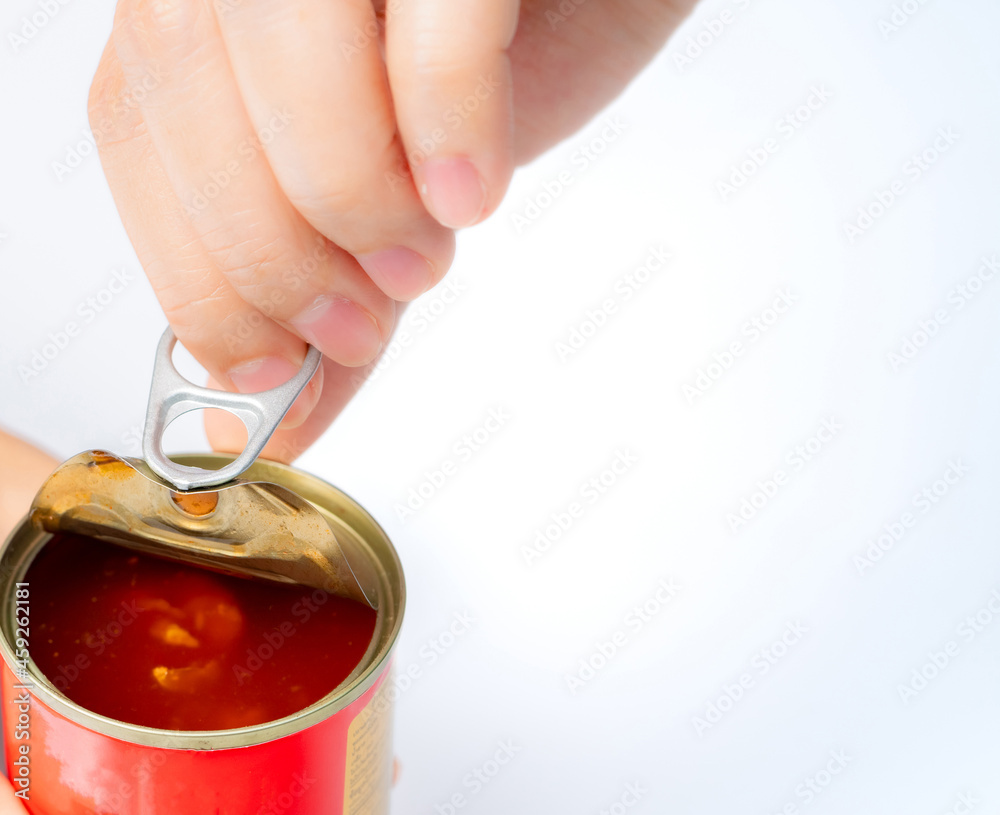 Woman's hand opens lid of canned fish on white background. Sardine in ...