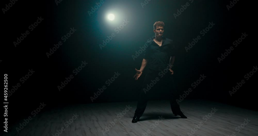 A professional experienced man is dancing on a dark stage lit by a lamp ...