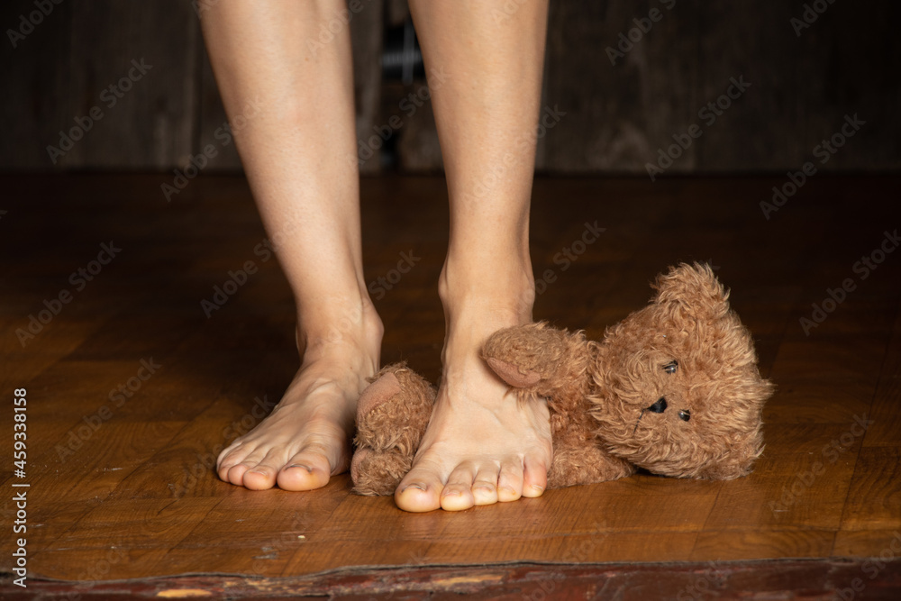 female bare feet stepping on a brown teddy bear on the old floor in a ...