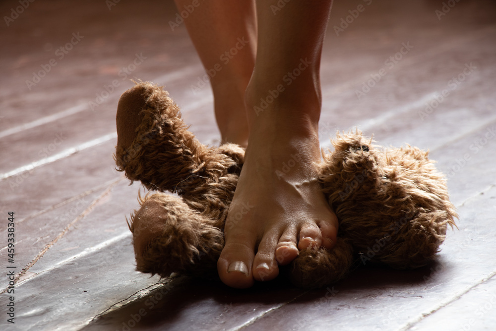 female bare feet stepping on a brown teddy bear on the old floor in a ...