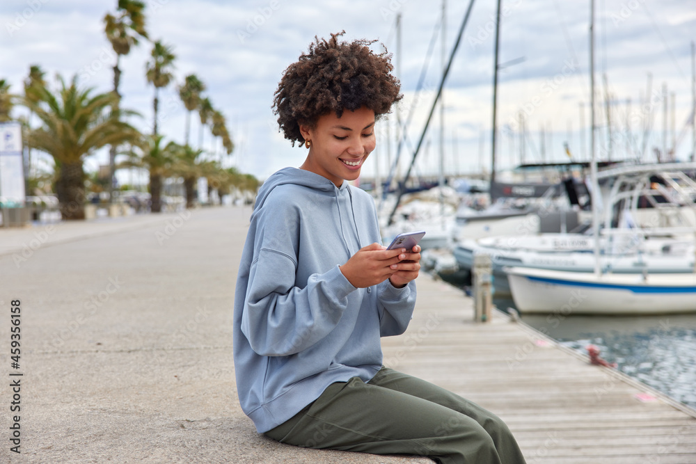 Glad Curly Haired African American Woman In Casual Clothes Sits At