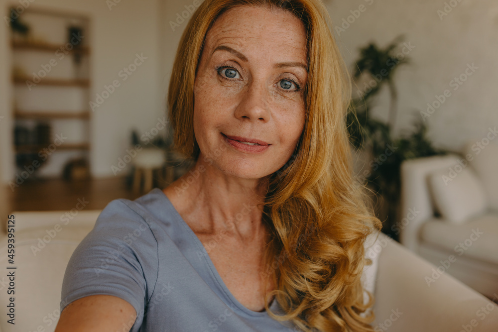Selfie of middle-aged ginger head long-haired woman doing selfie at home, posing with happy ...