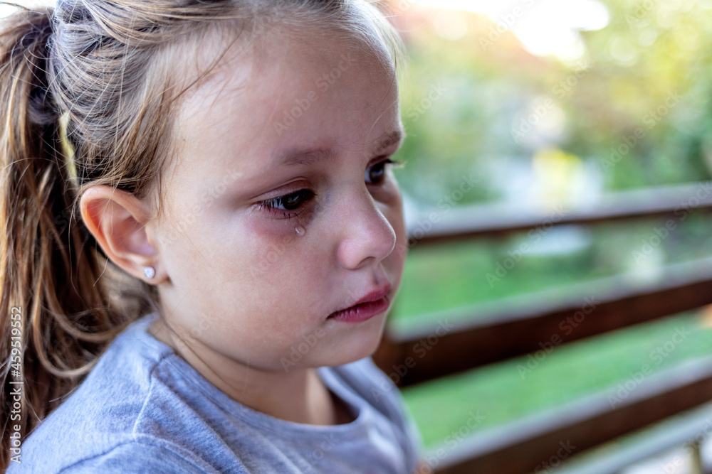 Sad crying Caucasian little girl looking away. Unhappy cute kid cries quietly as a tear begins ...