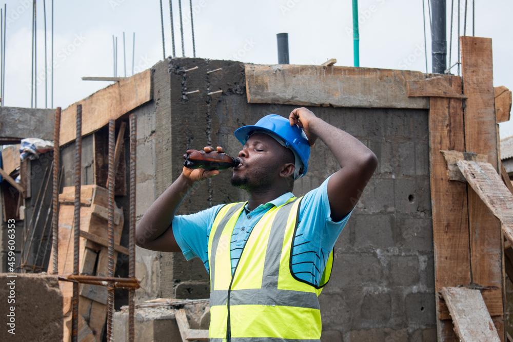 A thirsty male African construction worker drinking from a bottle on a ...