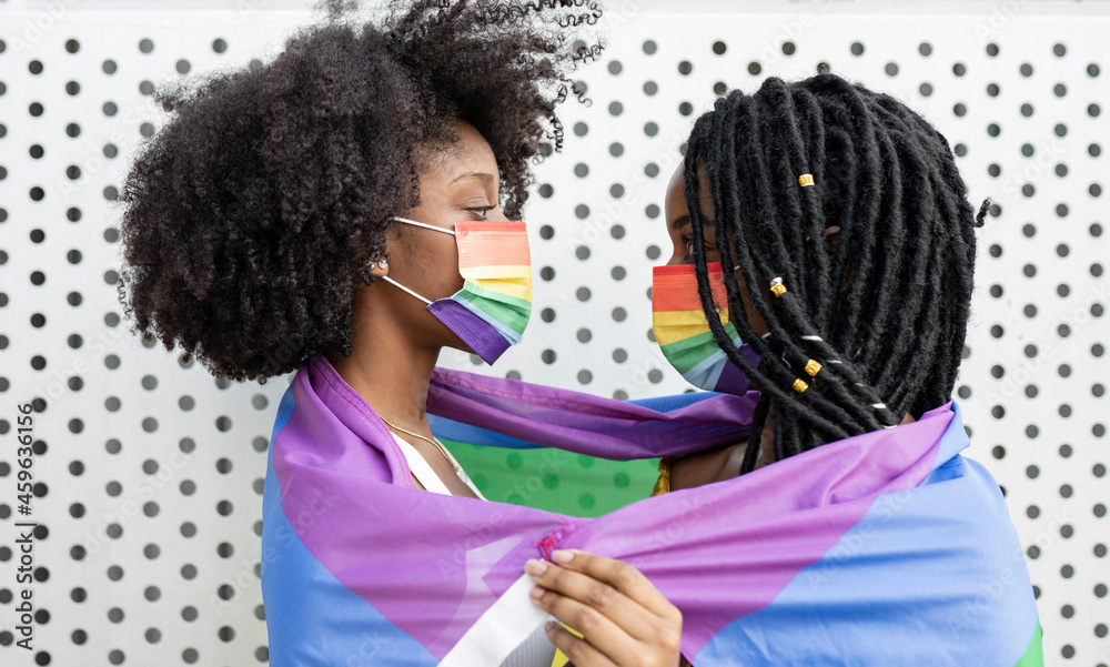 Young lesbian couple wrapped in pride flag during COVID-19 Stock Photo ...