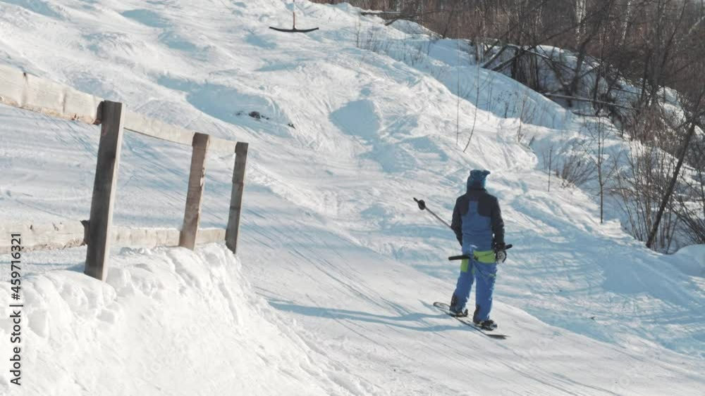 Snowboarder start climbing to the hill or a mountain using a T-bar lift ...