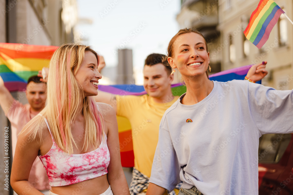 Young lesbian couple walking with rainbow flags during pride parade ...