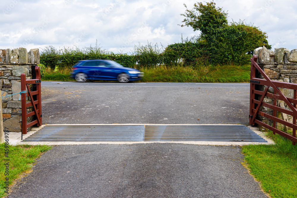 Car speeds past a laneway entrance with wooden gates and a cattle grid ...