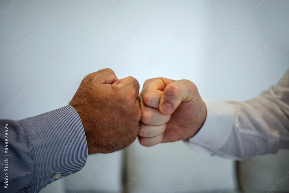 Shot of two unrecognisable men bumping fists against a white background ...