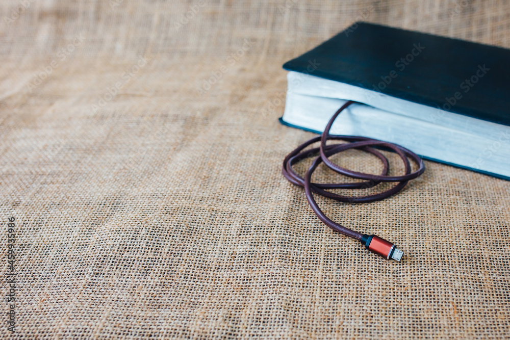 Close up of a smart phone cable connect to the holy bible on brown on ...