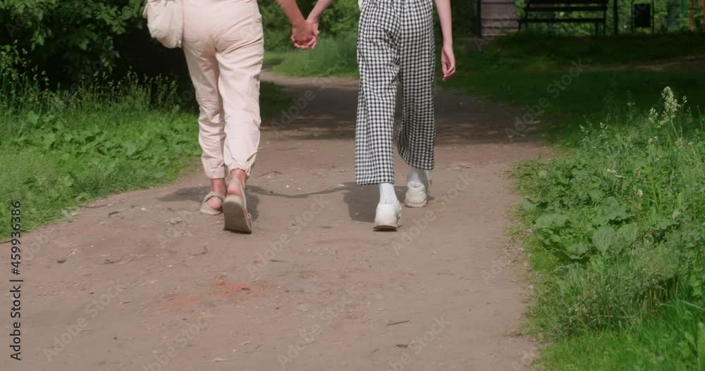 Rear view legs of two young girls walking together on pathway between ...