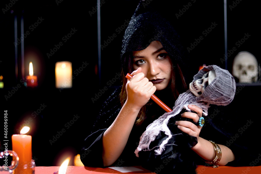 Dark witch in black hood casting curse on magical voodoo puppet ...