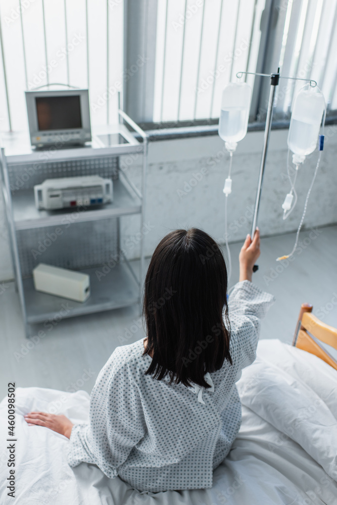 back view of patient sitting on hospital bed and holding hand on drop ...