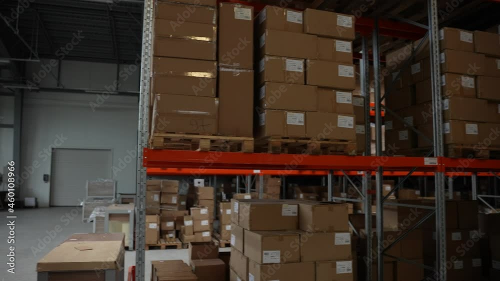 Operator of storehouse loader riding between rows of racks filled with ...