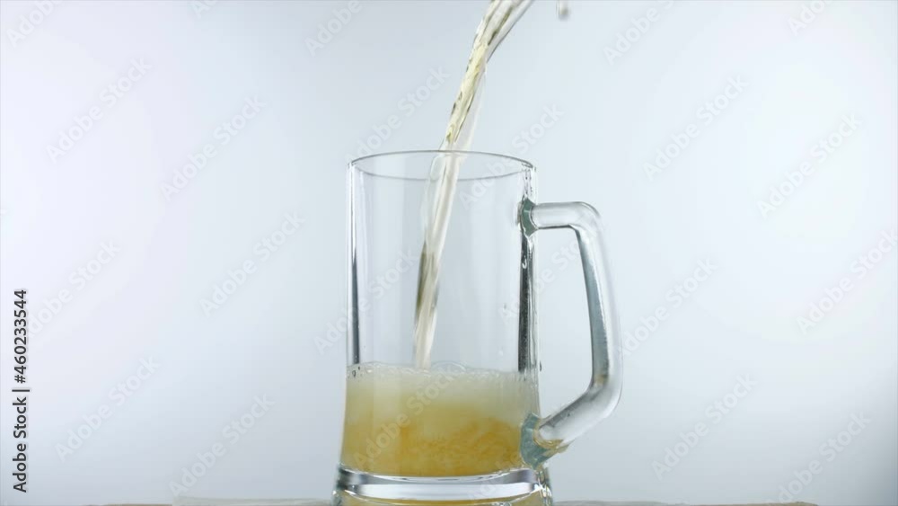 Pouring chilled beer from a brown bottle into a transparent glass ...