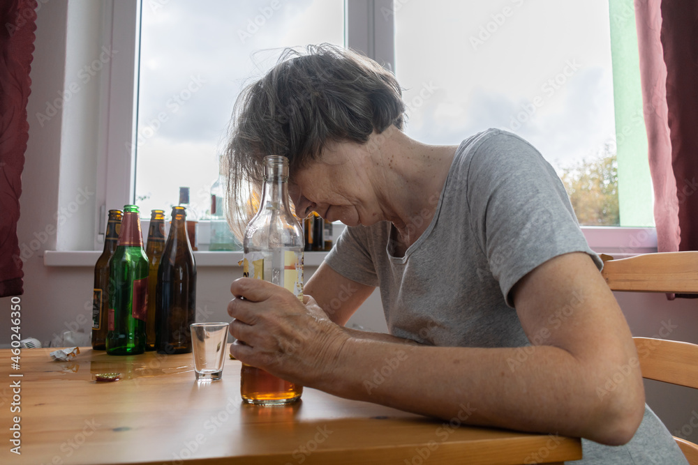 Foto de old senior female woman sit next to table drink alcohol bottle at home sad alone ...