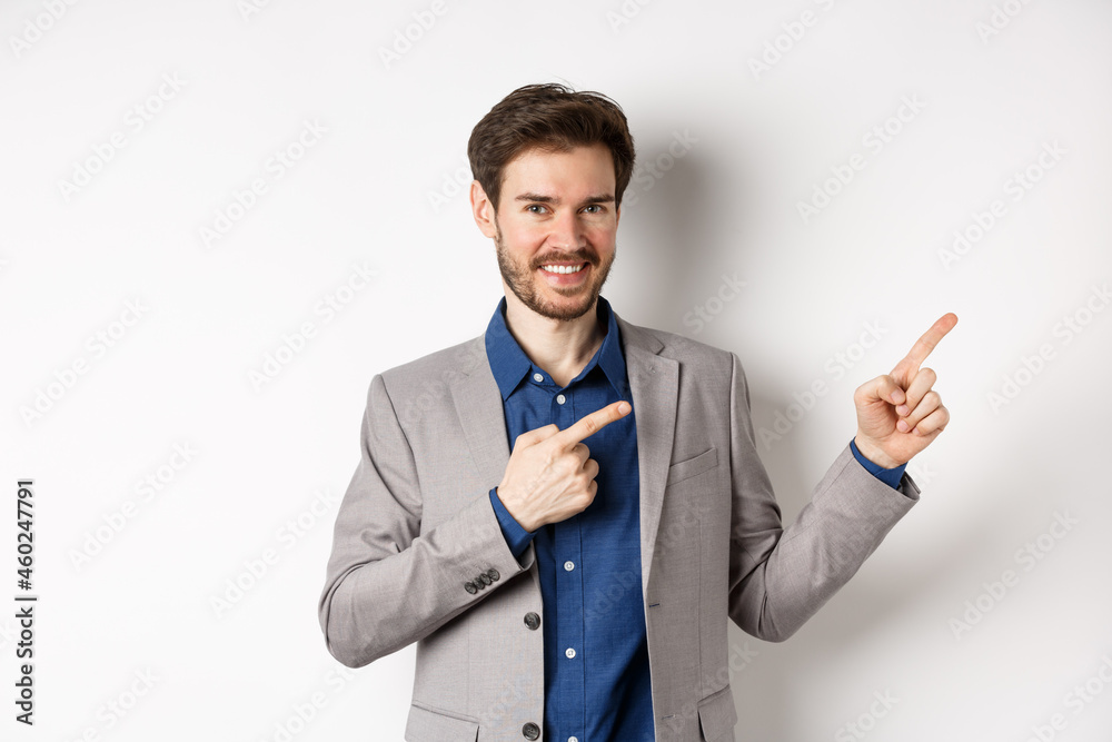 Handsome smiling man in business suit pointing fingers at upper right ...