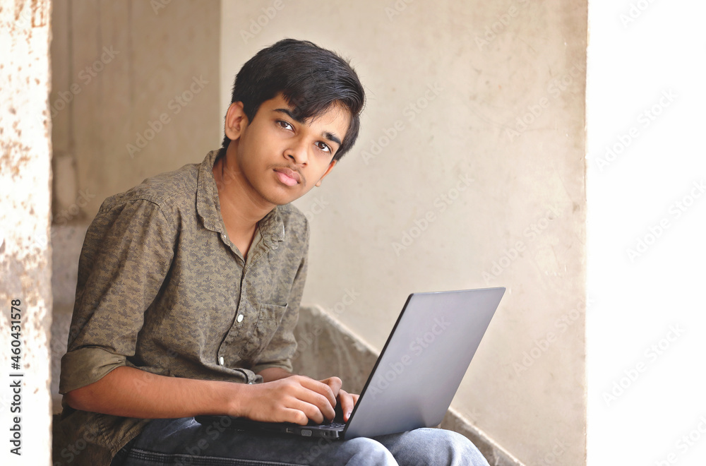 Indian boy using a laptop while attending the online classes at home ...