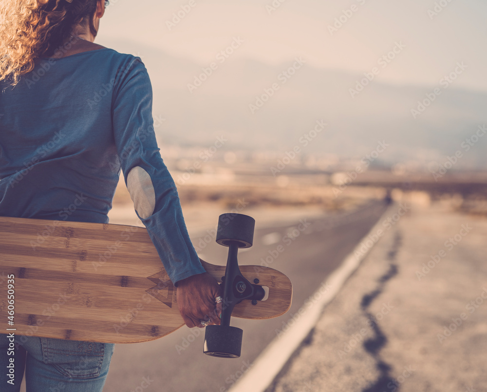Carefree woman standing and holding wooden longboard behind her back on ...