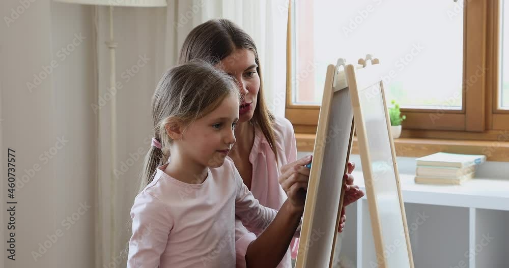 Smiling young mother give art lesson to little girl stand by drawing ...