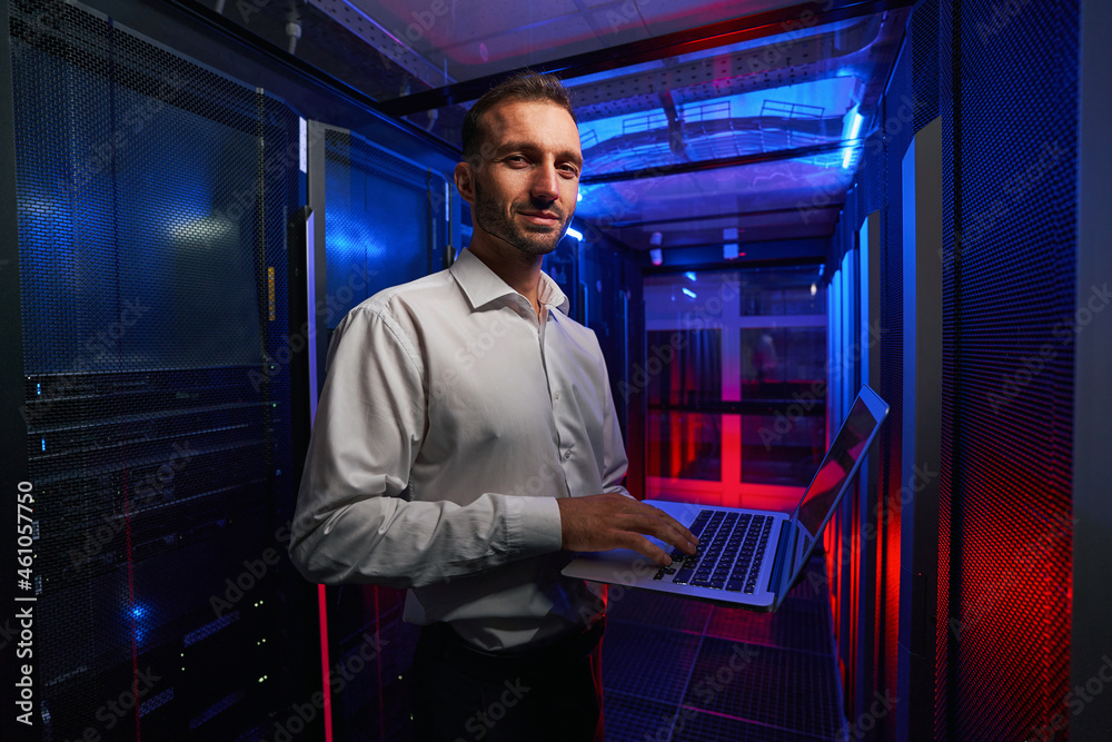 Bearded smiling system administrator is working with server rack and ...