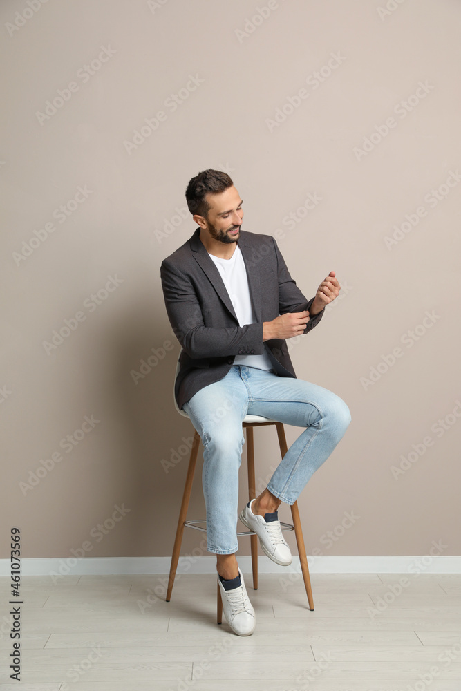 Handsome man sitting on stool near beige wall 素材庫相片 | Adobe Stock