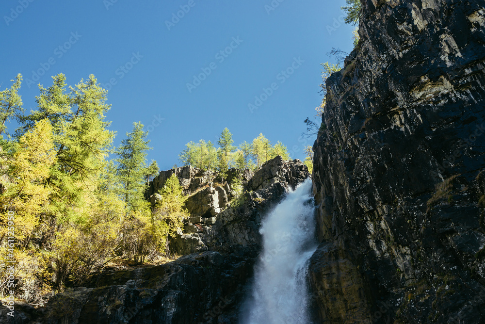 Scenic autumn landscape with vertical big waterfall and yellow trees at ...