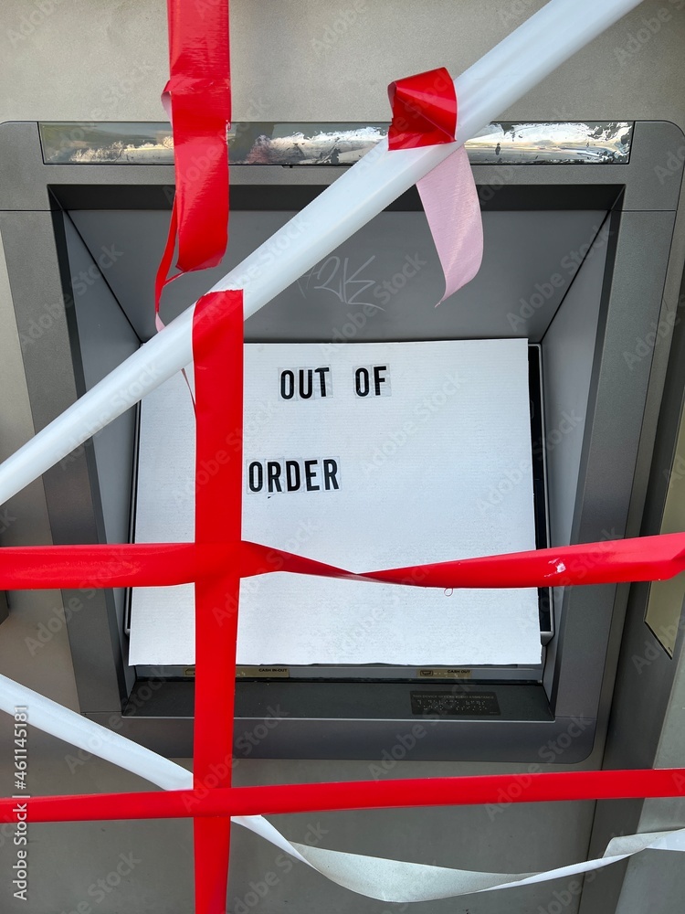 A broken atm machine covered in red tape with an out of order sign ...