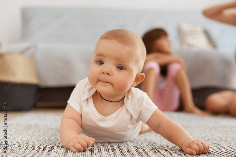 Indoor shot of cute baby wearing white clothing lying on floor on ...