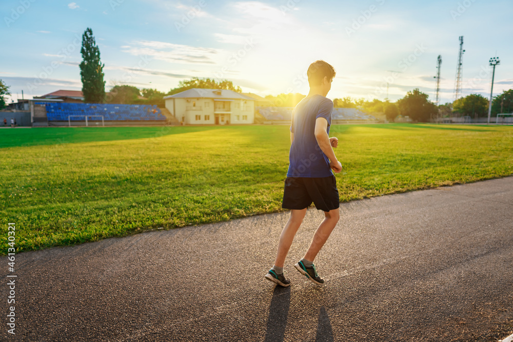 teen boy running along the stadium track, a soccer field with green ...