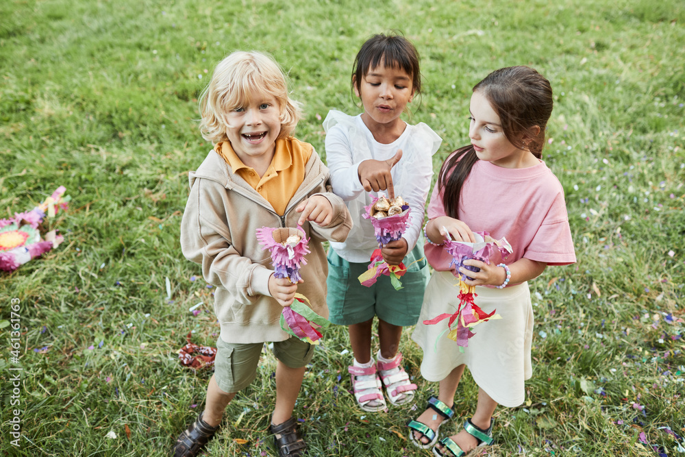 Full length portrait of three cute children holding sweets from pinata ...