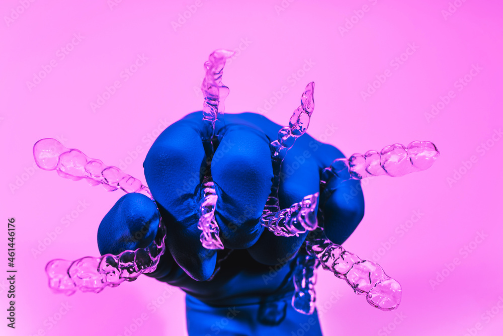 Invisible dental braces are held by a hand in a blue glove on a pink ...