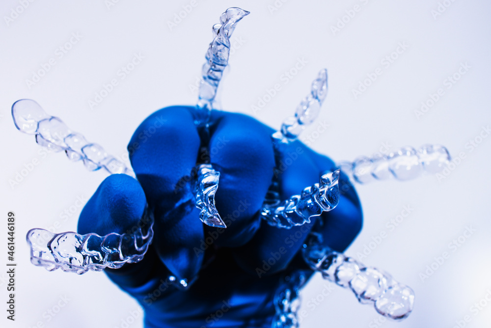 Invisible dental braces are held by a hand in a blue glove on a white ...