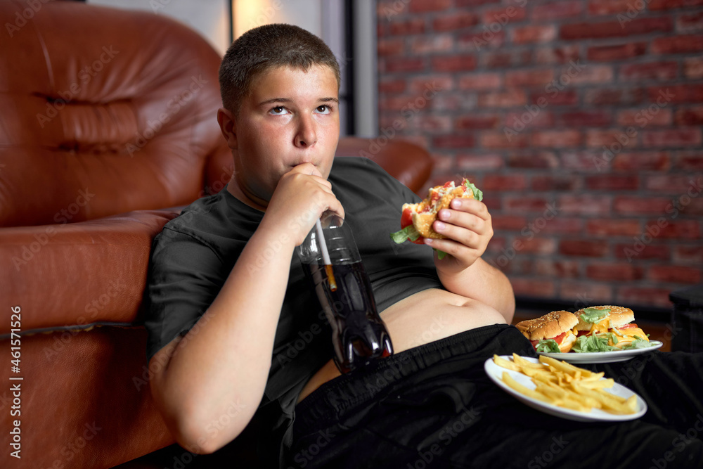 hungry caucasian fat boy is eating junk food at home while watching tv ...