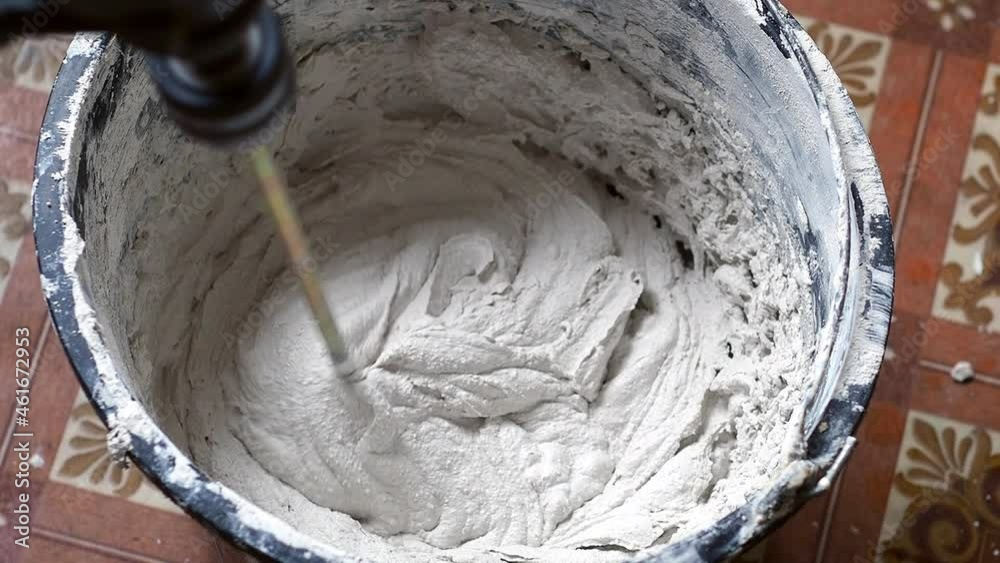 A person mixes cement and water in a container to get the finished ...