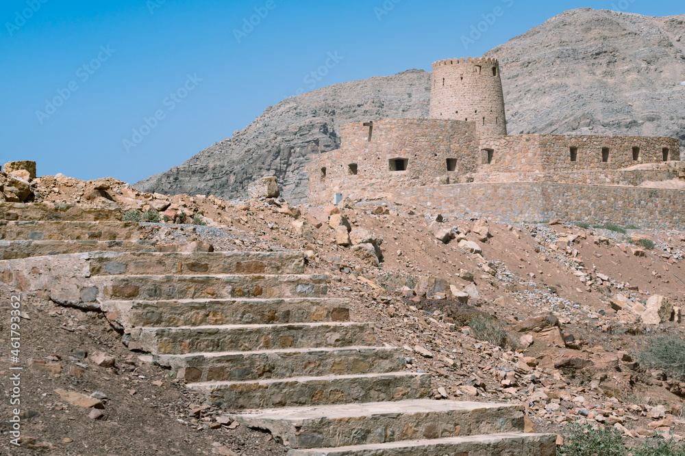 Stone walls of small medieval Arabian fort under tall mountain cliffs ...