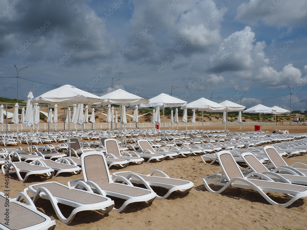 Wet sunbeds and umbrellas on the sea beach during heavy rain storm ...