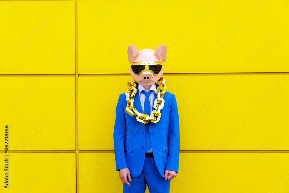 Man wearing vibrant blue suit, pig mask and large golden chain standing ...