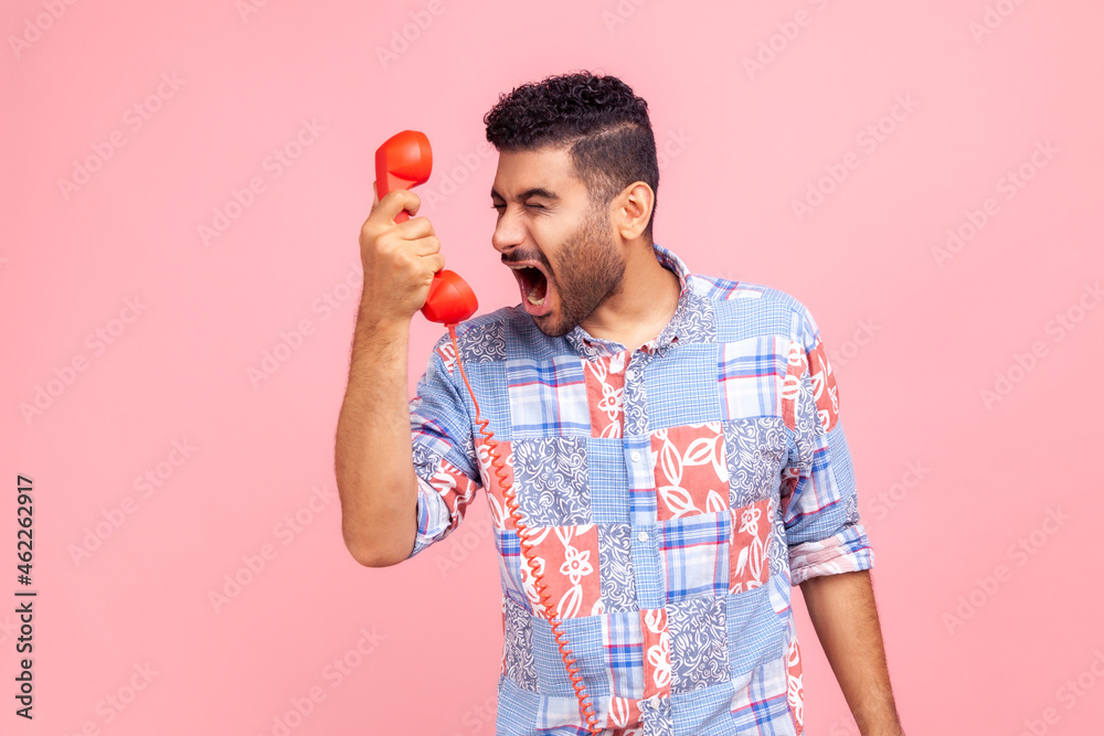 Portrait of bearded angry man screaming into phone handset, annoyed by ...