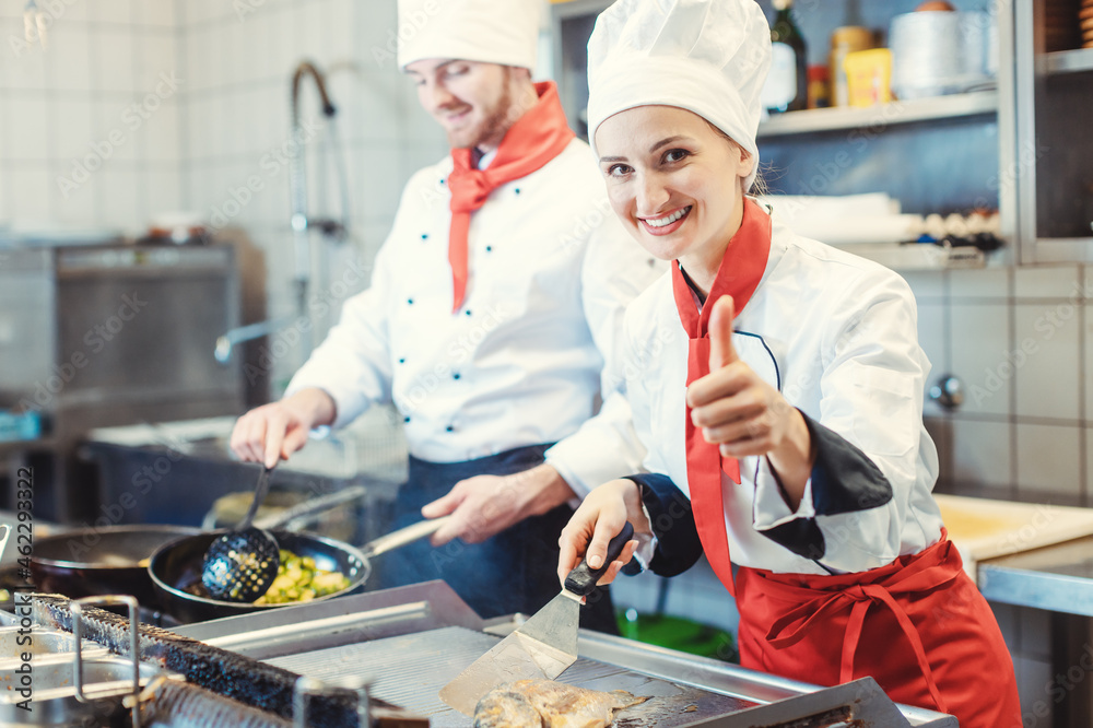 Chefs in restaurant kitchen cooking and giving the thumbs up as a sign ...
