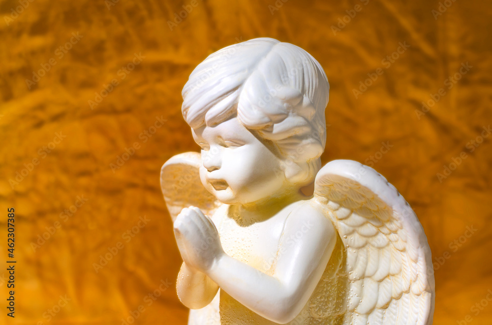 White angel boy sculpture near the firelight with golden shadows on the ...