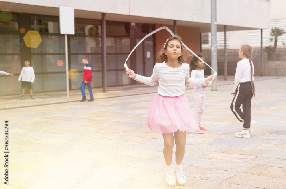 Cute tween girl in pink skirt jumping rope in school yard during recess ...