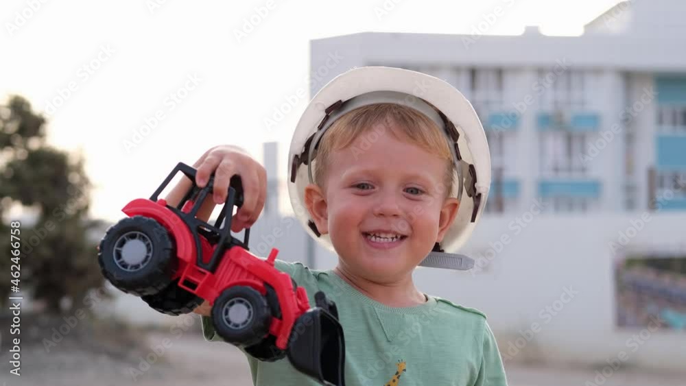 A little boy in a white helmet is holding a toy red loader. A child on ...