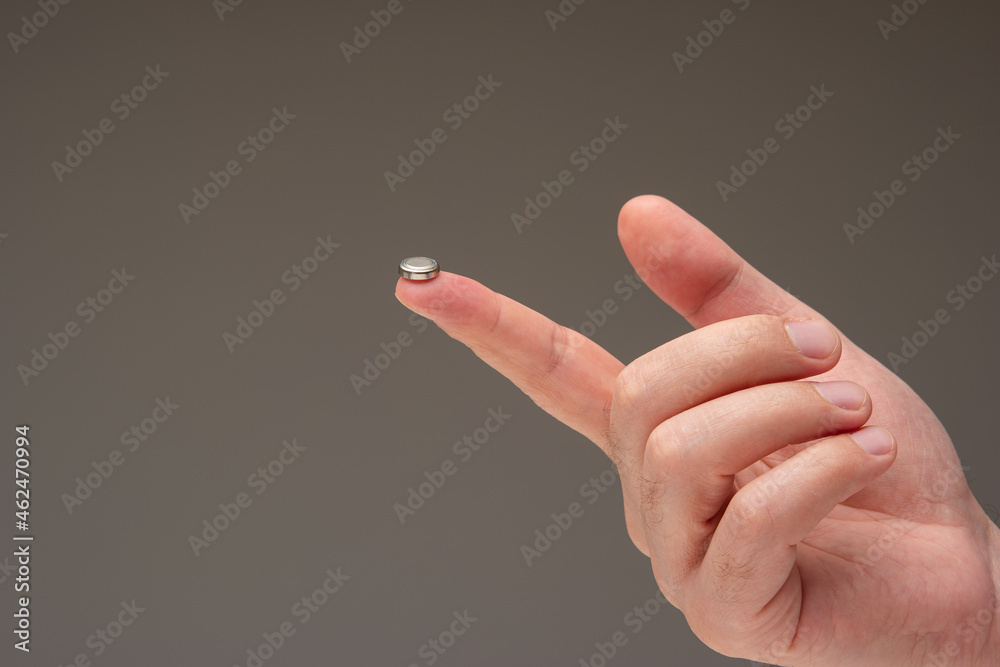 Very small button L1131 battery cell set on Caucasian male's index ...