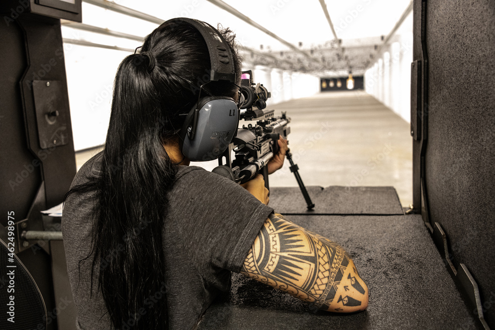 View of a young woman shooting a rifle on a stand at a shooting range ...