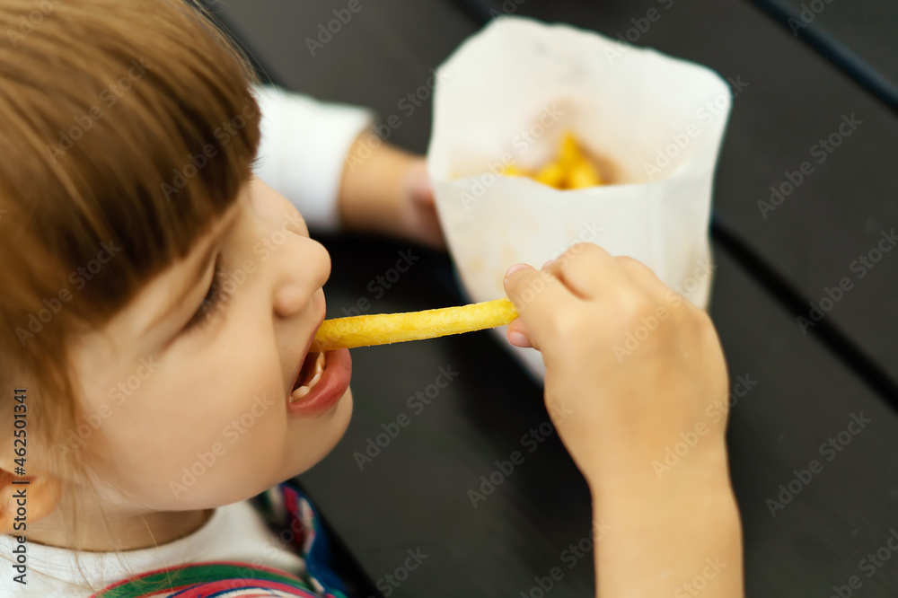 Close-up of a pretty little girl eating delicious French fries while ...