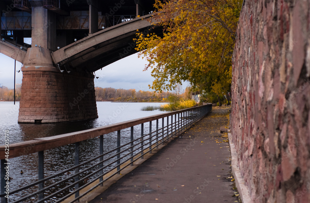 sidewalk with railings along river. large stone bridge with arches ...