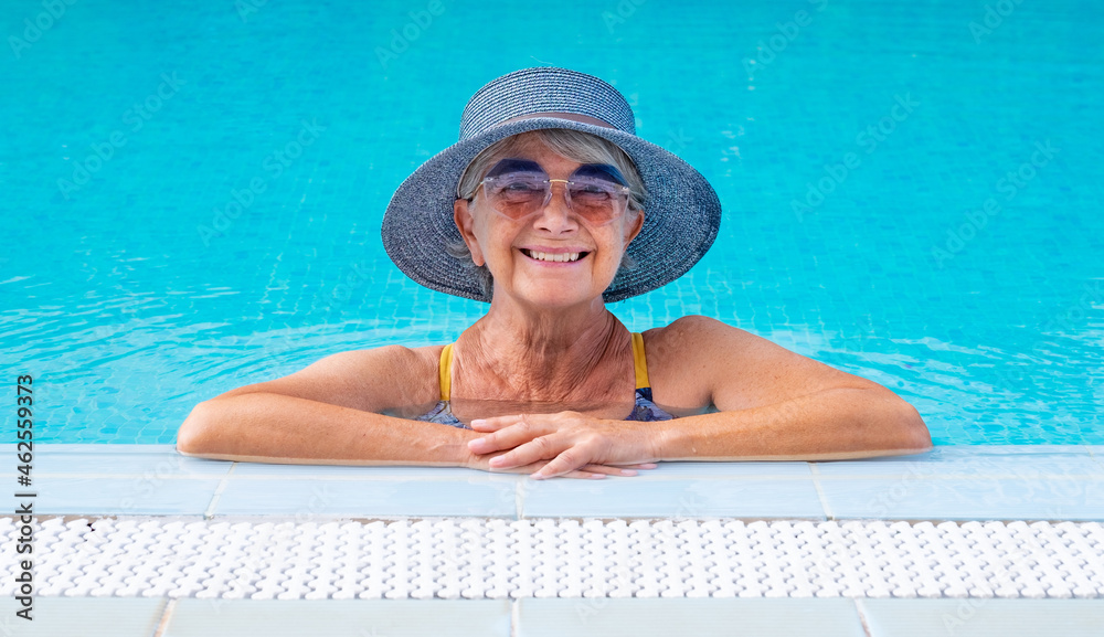 Smiling mature woman in outdoor swimming pool standing near the edge ...