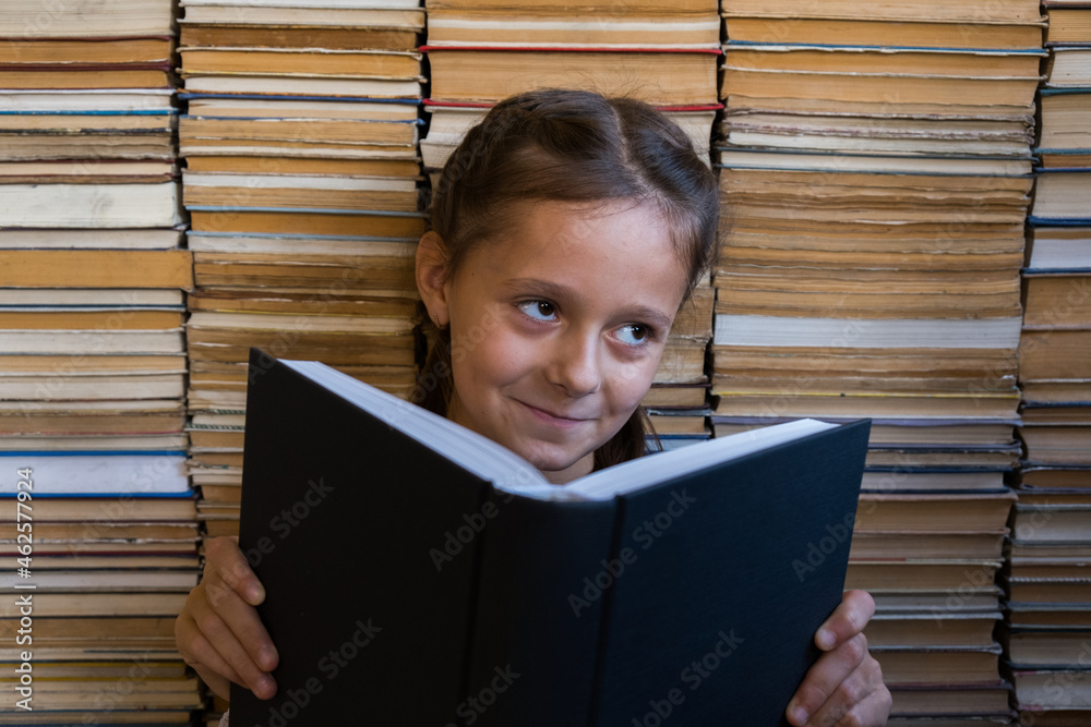 Curious cute preschool kid girl sitting with a book, on books ...